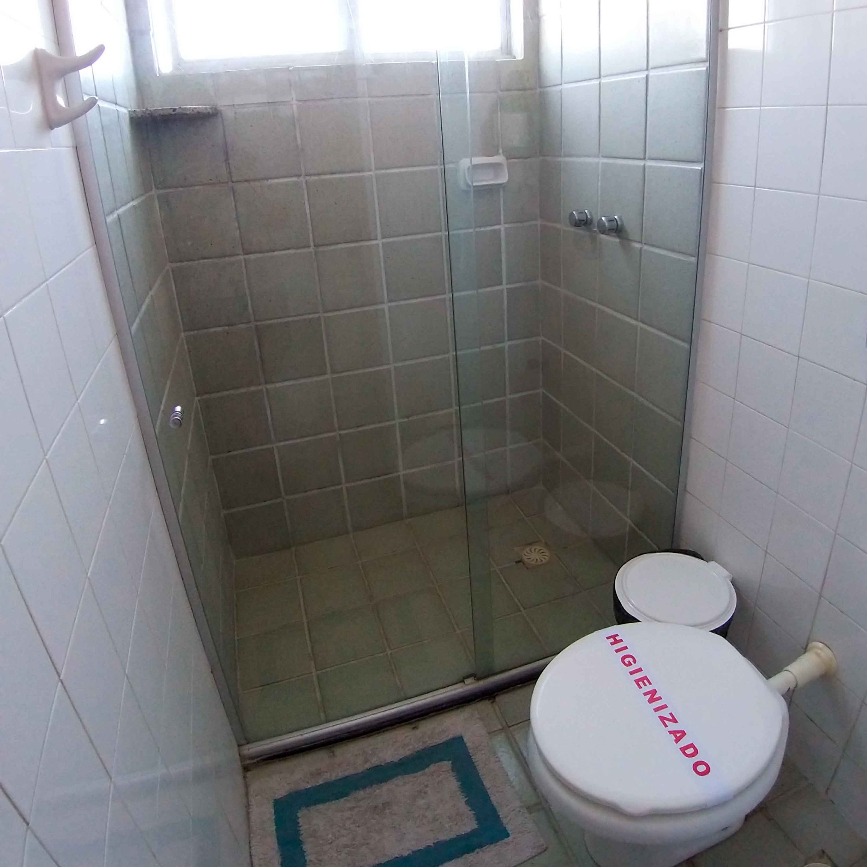 Casa de banho com chuveiro em cabine de vidro, sanita e um pequeno armário com artigos de higiene pessoal.