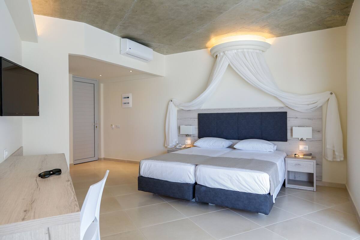 Um quarto moderno com uma cama grande, mesas de cabeceira, uma TV de tela plana e um ventilador de teto.
