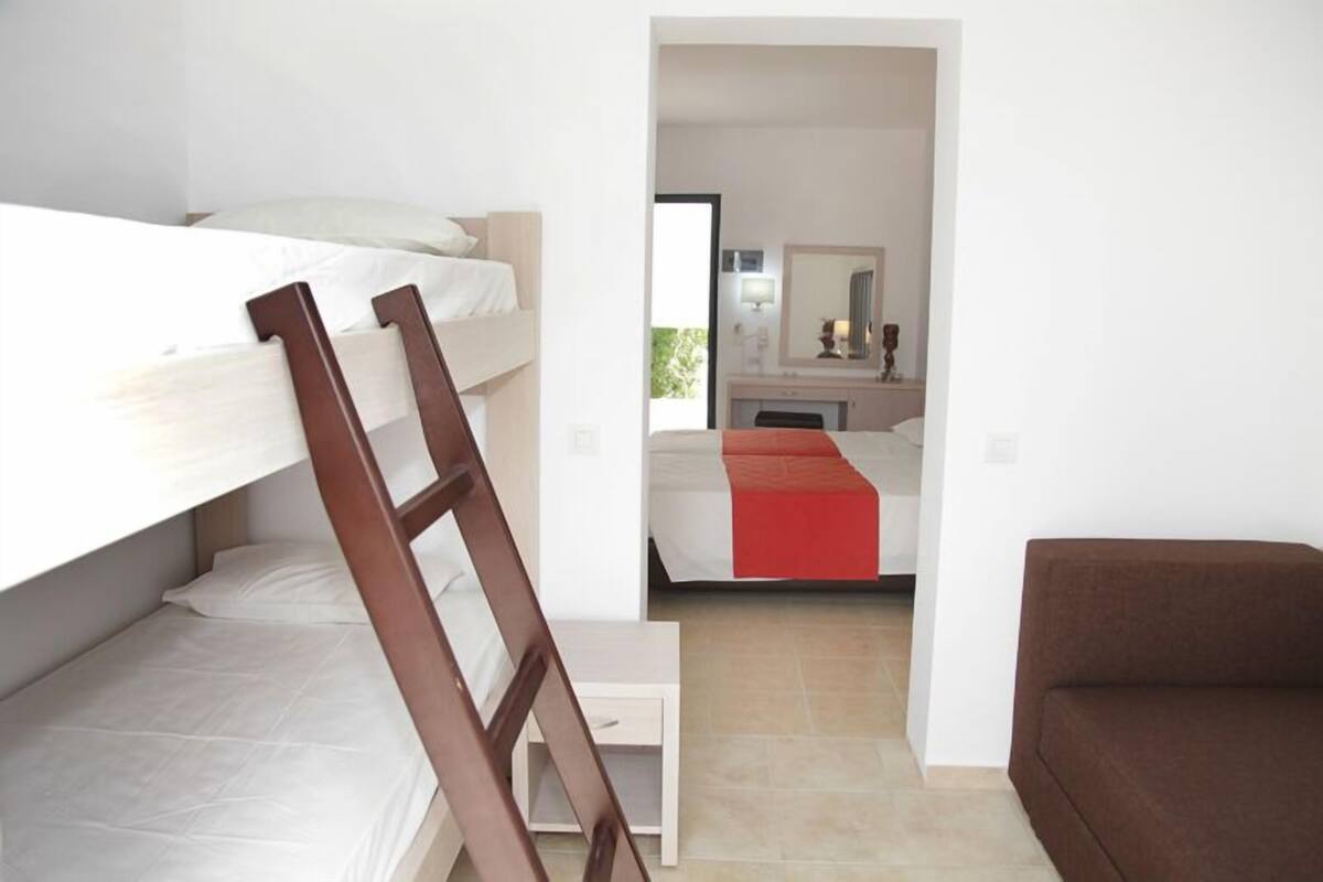 Quarto com cama de solteiro, escrivaninha, espelho e sofá marrom.