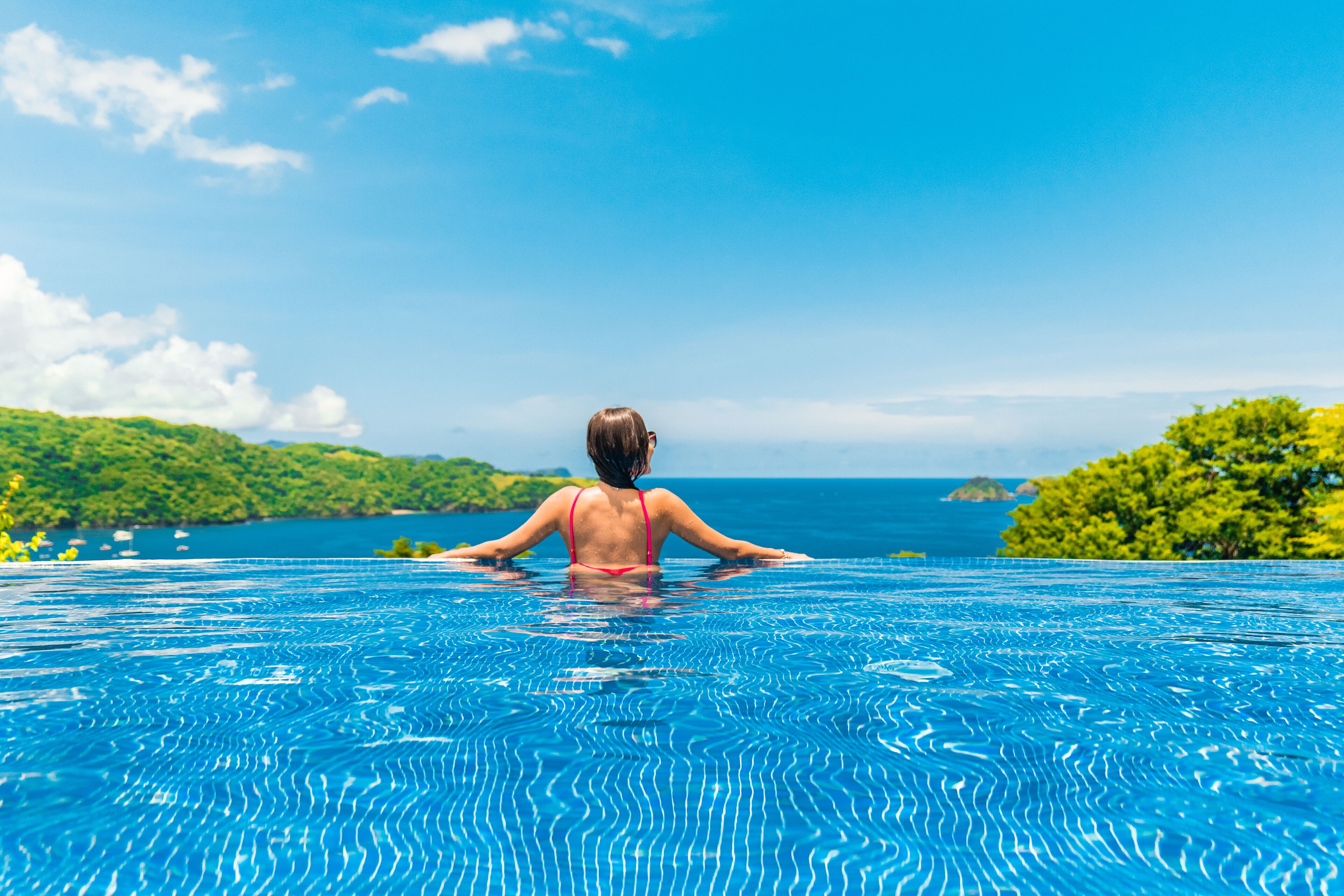 Uma pessoa em uma piscina com vista para o oceano e vegetação.