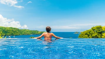 Uma pessoa em uma piscina com vista para o oceano e vegetação.