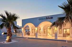 Um edifício moderno com o nome 'aquablue' em destaque. Apresenta uma série de arcos e uma área de estar ao ar livre coberta.