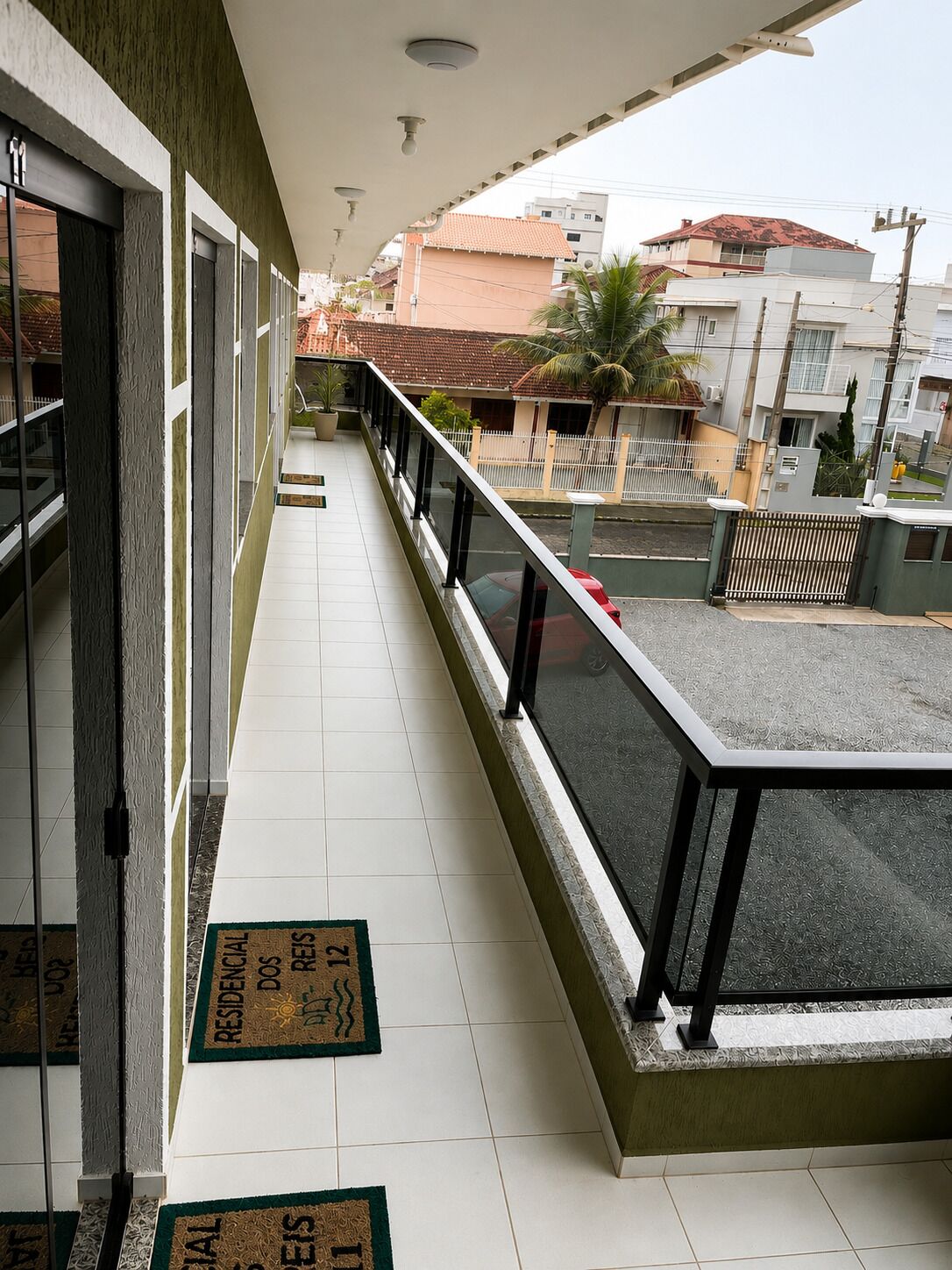 Uma varanda com guarda-corpo, piso de azulejos e vista para a rua e edifícios.