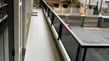 Uma varanda com guarda-corpo, piso de azulejos e vista para a rua e edifícios.