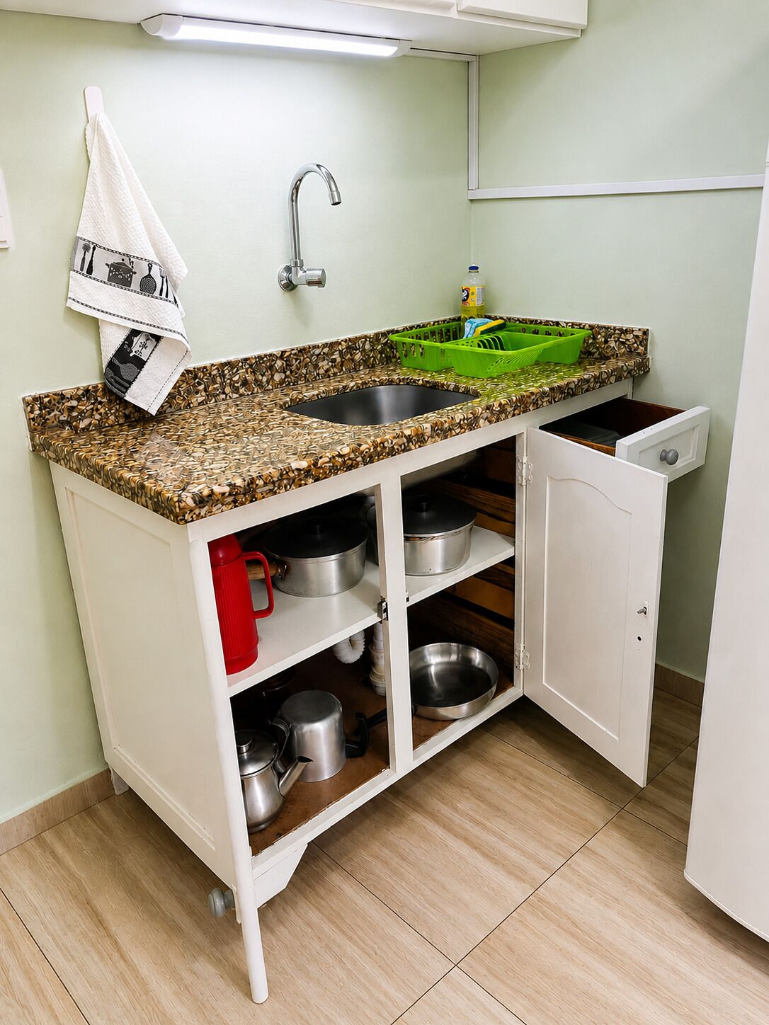 Cozinha compacta com bancada de granito, pia, escorredor de louça e armário com panelas e frigideiras.