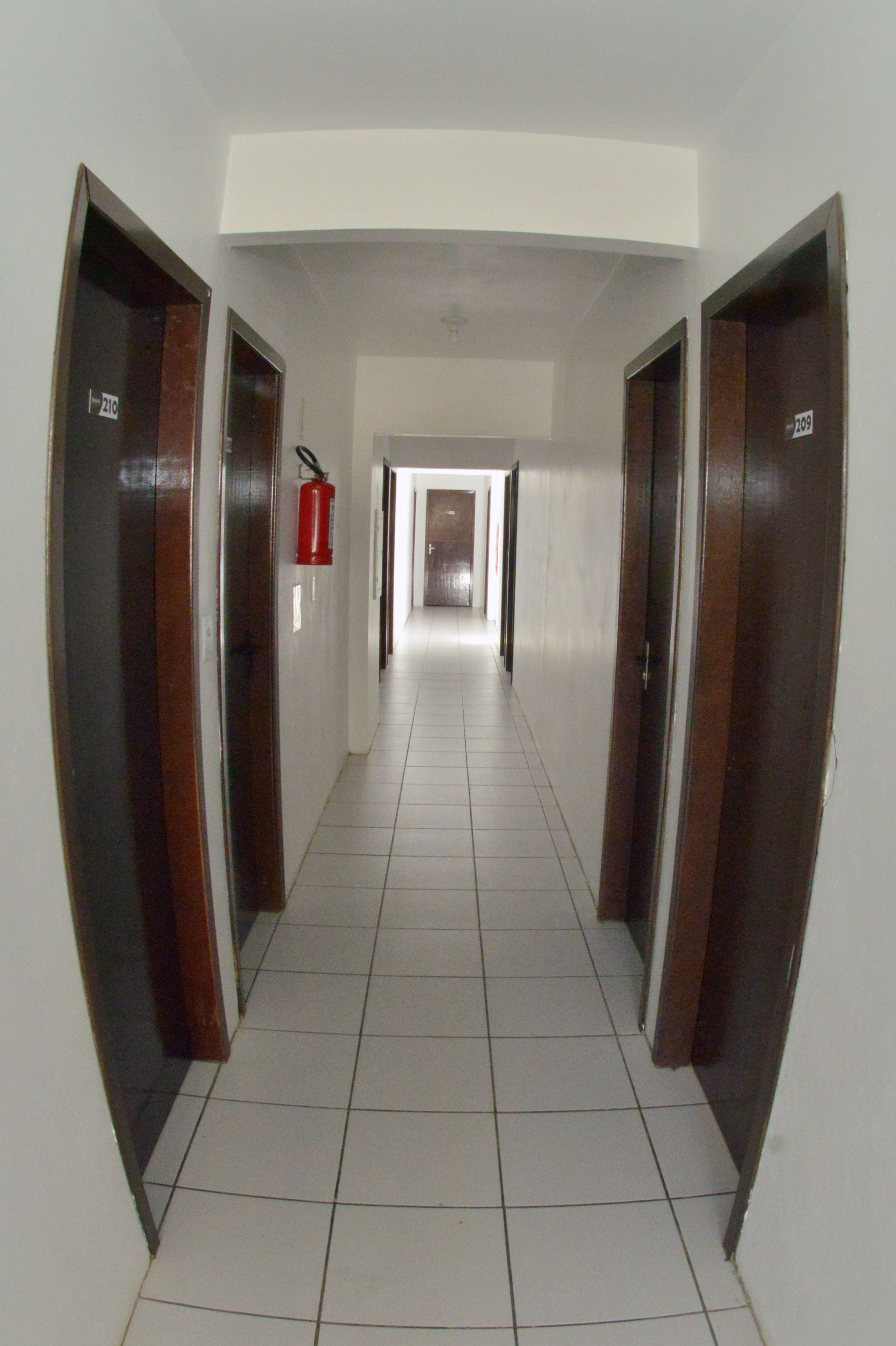 Um corredor longo e estreito, com portas de madeira em ambos os lados e um extintor fixado na parede.