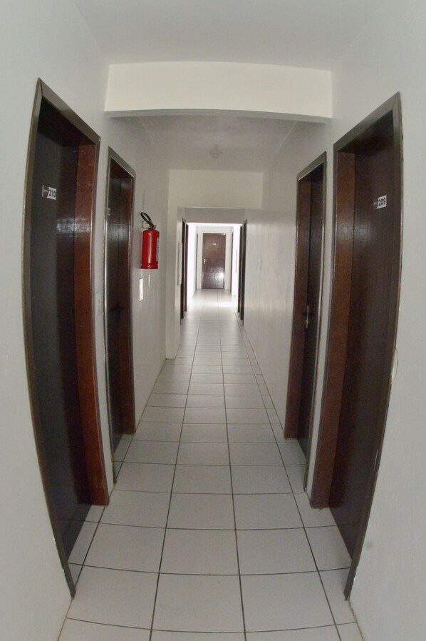 Um corredor longo e estreito, com portas de madeira em ambos os lados e um extintor fixado na parede.