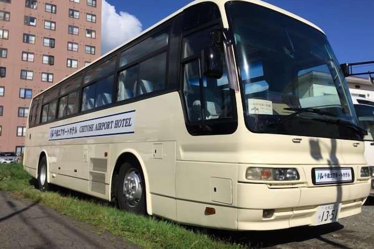 Um ônibus com a inscrição "CHICAGO AIRPORT HOTEL" na lateral, estacionado na grama com um edifício ao fundo.