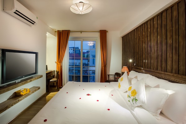 Quarto de hotel com uma cama grande, uma televisão de tela plana, uma cabeceira de madeira e vista para edifícios pela janela.