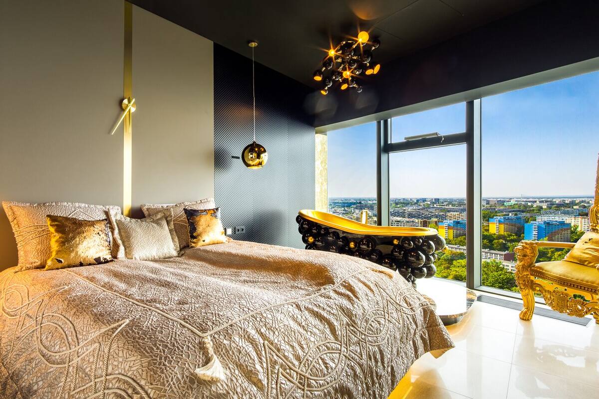 Quarto moderno com uma cama grande, vista da cidade através de amplas janelas e um lustre exclusivo.