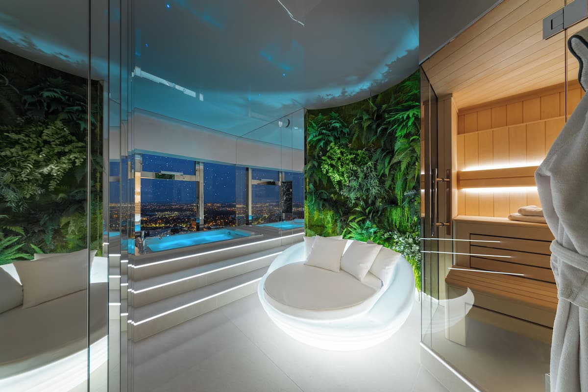 Um banheiro moderno com hidromassagem em vidro, uma área de estar circular e uma parede com plantas verdes ao fundo.