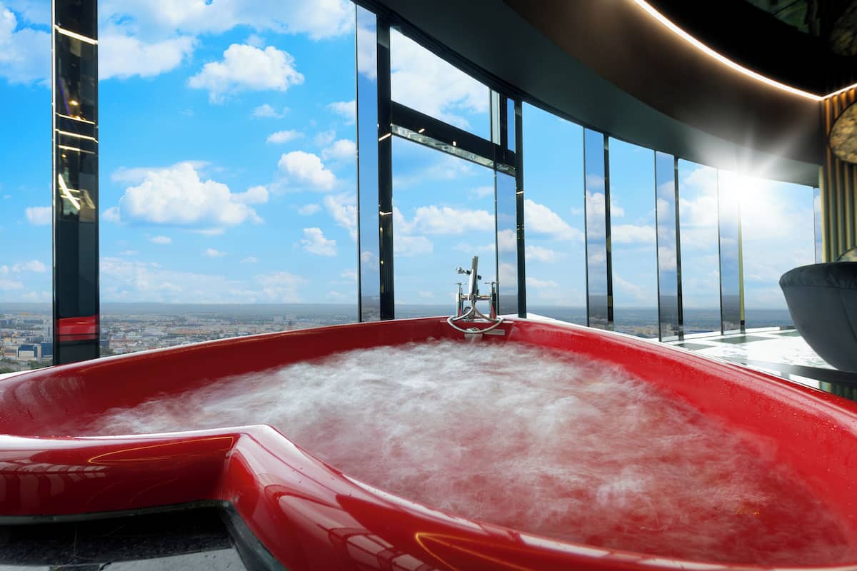 Uma banheira de hidromassagem vermelha com vista para a cidade através de grandes janelas.