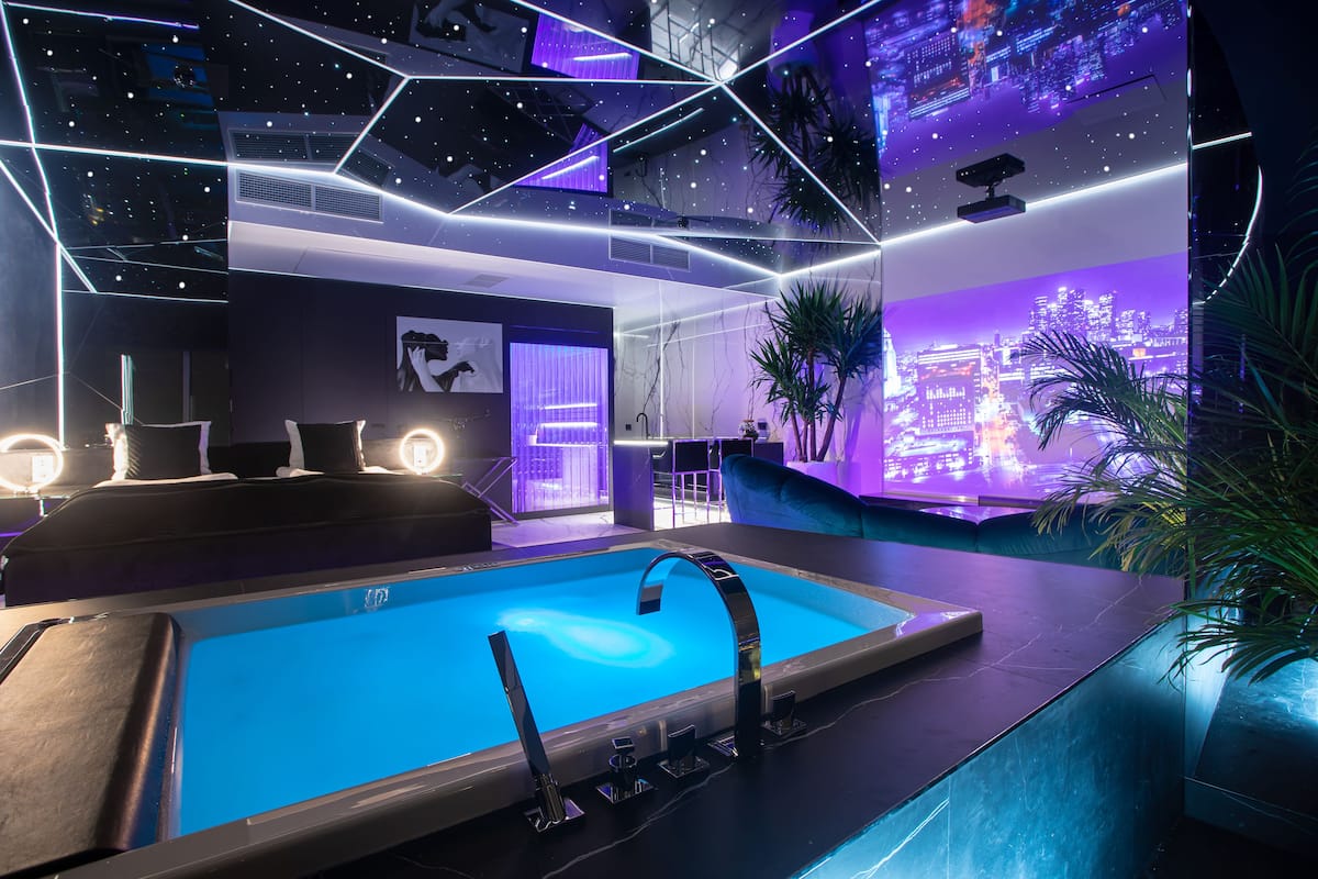 Área moderna de piscina interna com exibição digital de um horizonte urbano, iluminação geométrica e um espaço de estar com vista para a piscina.