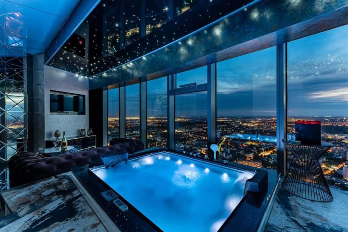 Quarto de hotel moderno em arranha-céu, com grande janela e vista para a cidade, banheira de hidromassagem privativa e design interior contemporâneo.