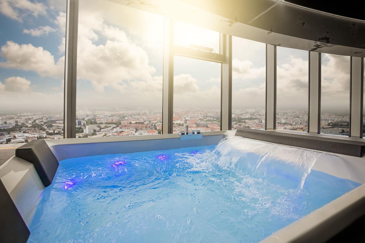 Banheira de hidromassagem com vista para a cidade através de grandes janelas.
