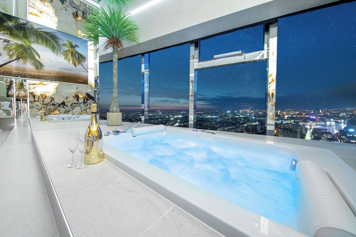 Um banheiro moderno com uma banheira grande, uma garrafa de champanhe e copos, com vista para a cidade à noite.