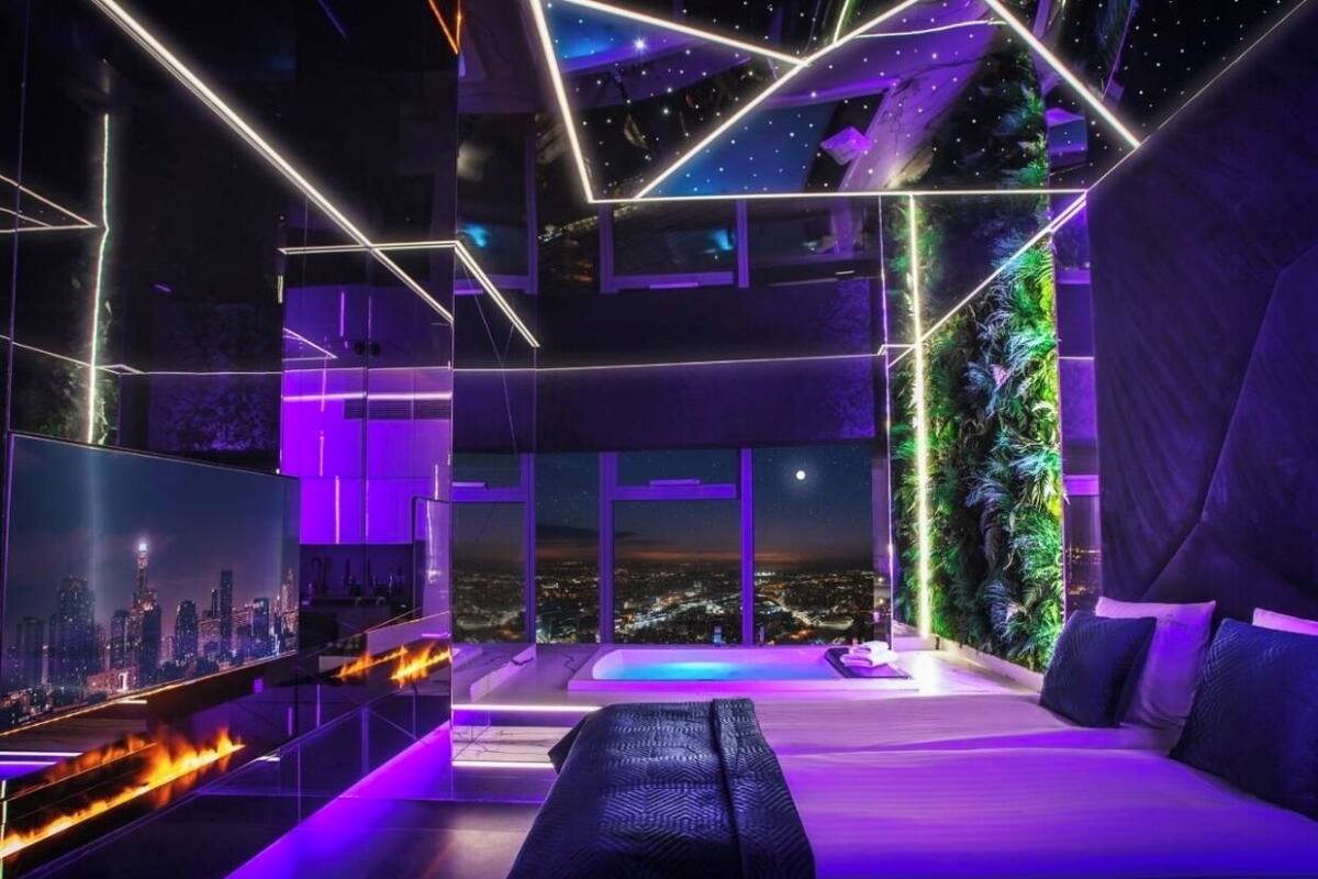 Quarto de hotel moderno com vista para a cidade, uma cama grande, área de estar e uma parede com jardim vertical.