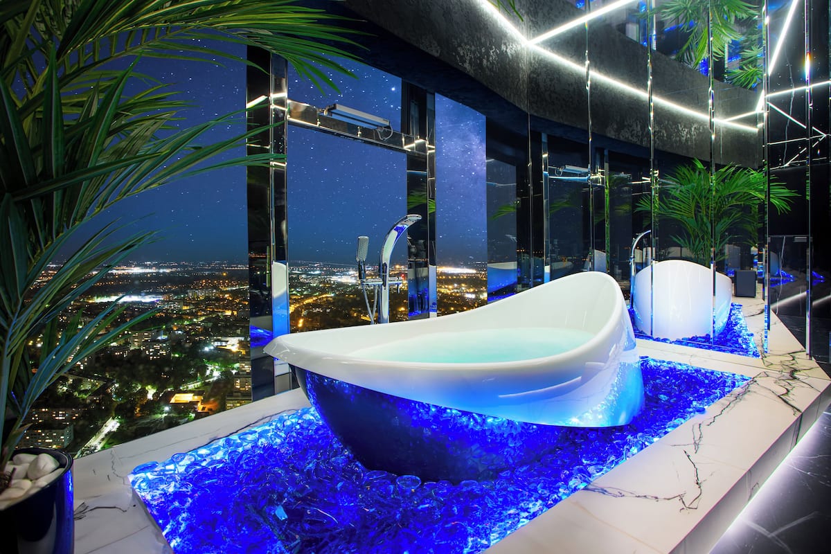 Uma casa de banho moderna com uma banheira grande, chuveiro e vista para a paisagem urbana à noite.