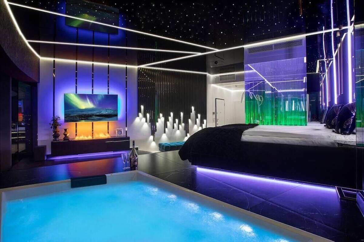 Quarto de hotel moderno com uma televisão grande, piscina e área iluminada em verde.
