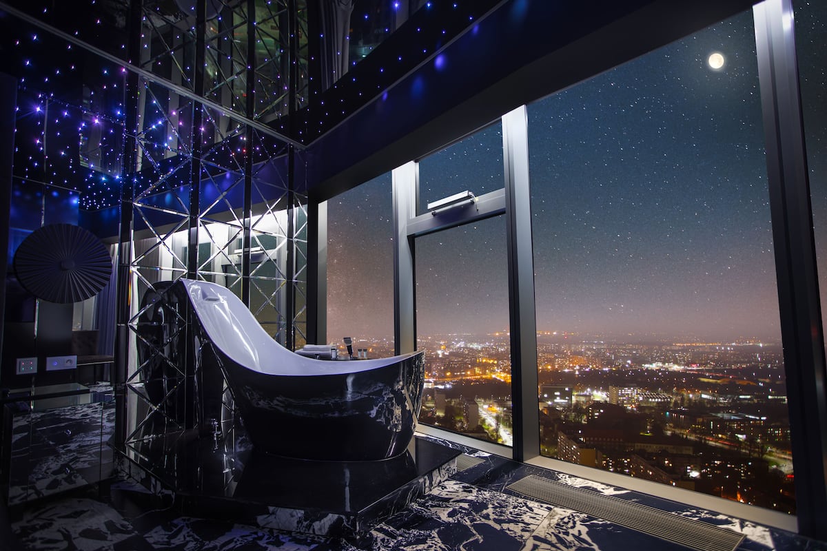 Casa de banho moderna com uma banheira grande, vista da cidade através de amplas janelas e céu estrelado à vista.