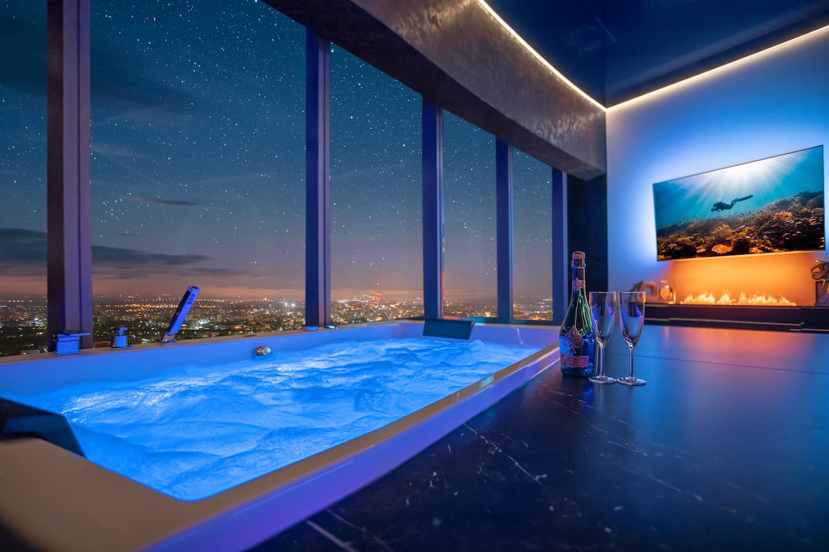 Quarto moderno com uma banheira grande, vista para a cidade, um quadro e uma lareira.