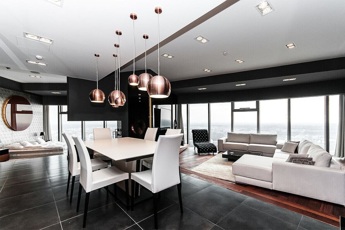 Uma sala de jantar moderna com uma mesa grande e cadeiras, um sofá e luminárias pendentes.