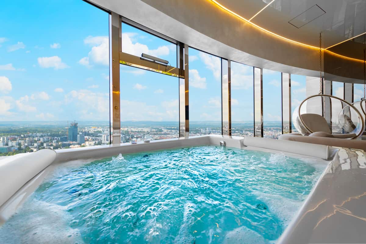 Uma banheira de hidromassagem com vista para a cidade, grandes janelas e uma cadeira suspensa.