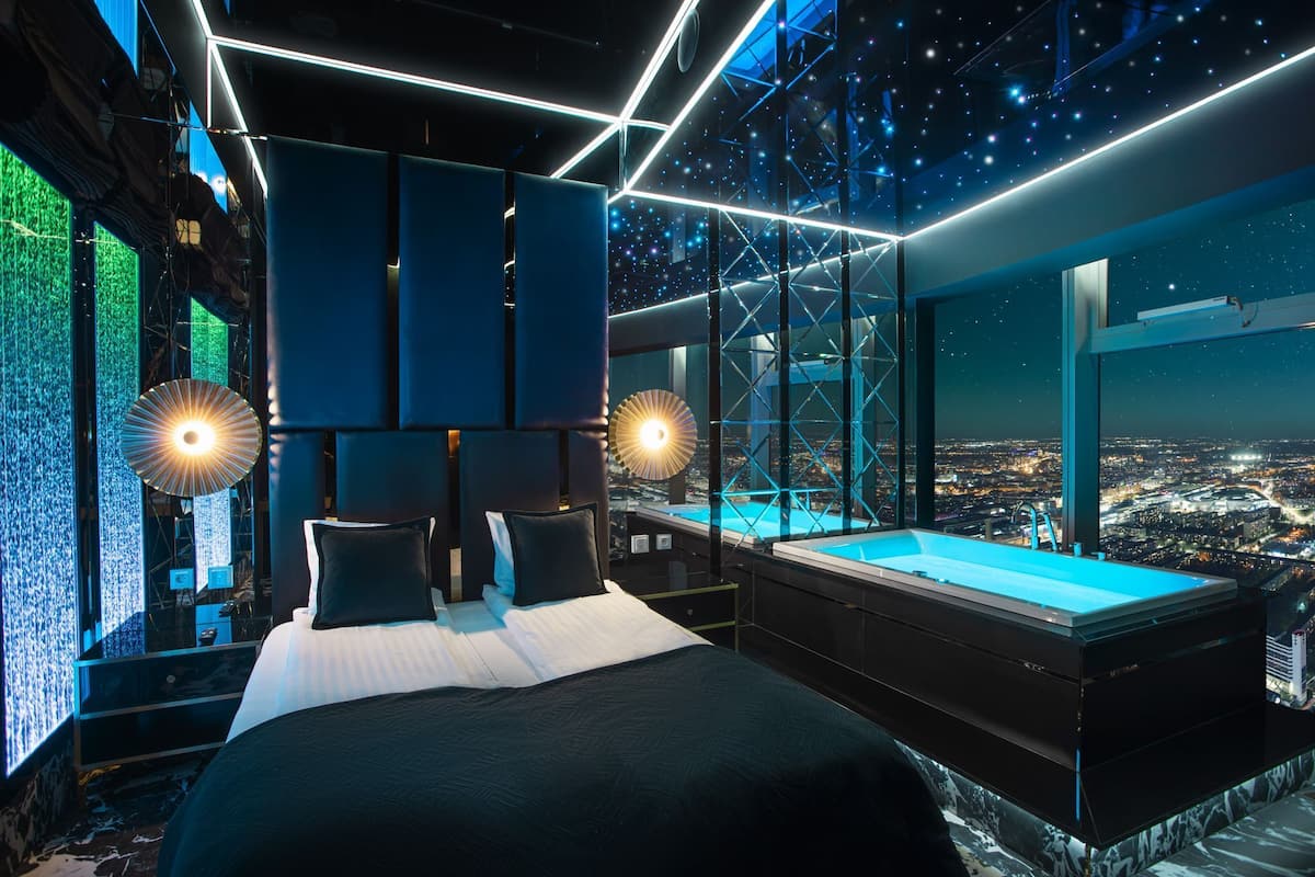 Quarto de hotel moderno com uma cama grande, jacuzzi e vista para a cidade.