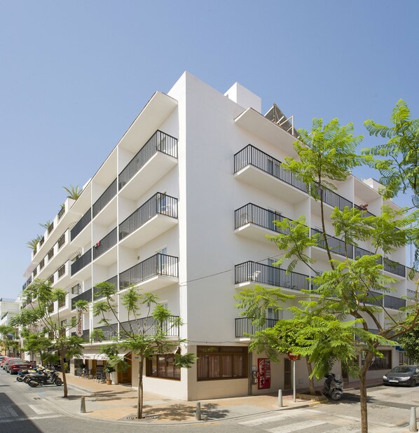 Um edifício com várias andares, varandas, uma rua na frente e áreas verdes.