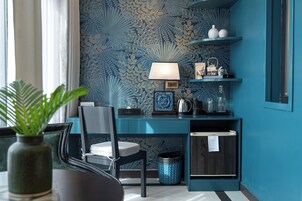 Quarto moderno com parede de destaque em tom de verde-água, uma escrivaninha com luminária, uma cadeira e uma lixeira pequena.
