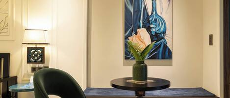 Um hall moderno com uma cadeira verde, uma pequena mesa redonda com um vaso e uma grande pintura abstrata na parede.