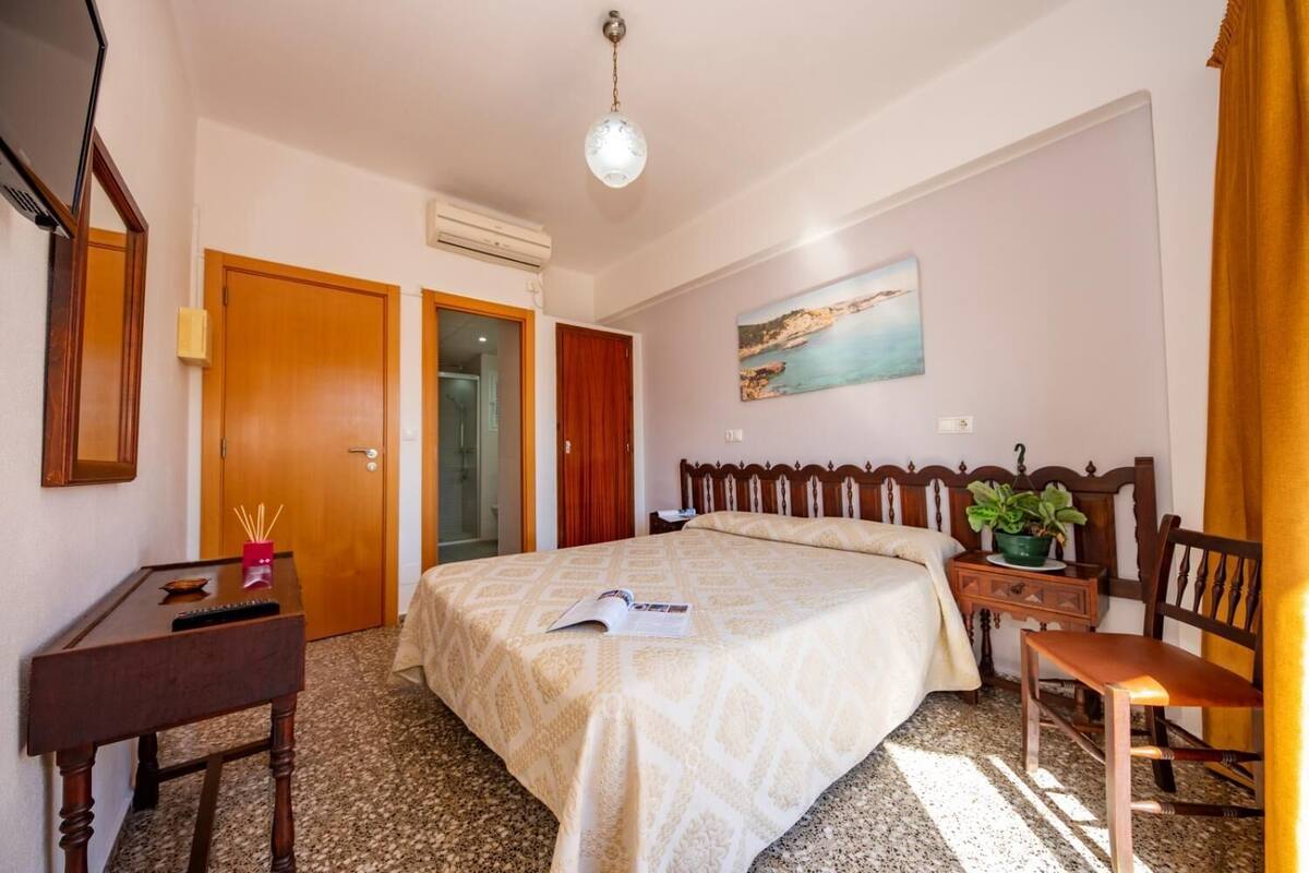 Quarto com cama, escrivaninha, cadeira, mesa de cabeceira com uma planta e um quadro na parede.