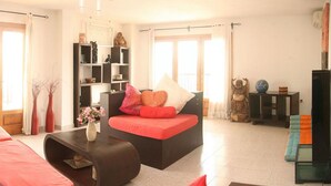 Uma sala de estar com um sofá vermelho, um sofá preto e uma mesa de centro. Há uma estante com objetos decorativos e uma estátua.