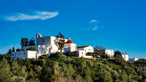 Um edifício branco com uma cúpula vermelha numa encosta, rodeado de árvores.
