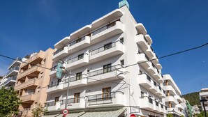 Um hotel com vários andares, varandas, um restaurante no andar térreo e um céu azul e límpido.