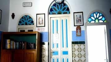 Quarto com uma estante de madeira, um relógio na parede, uma porta com listras azuis e brancas e uma janela com padrão azul.