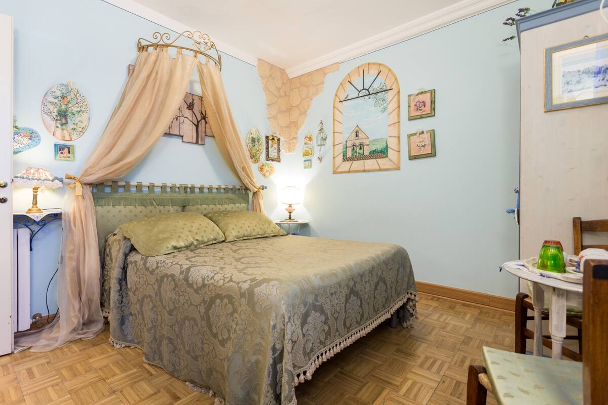 Um quarto com cama, mesa de cabeceira, mesa e cadeira.