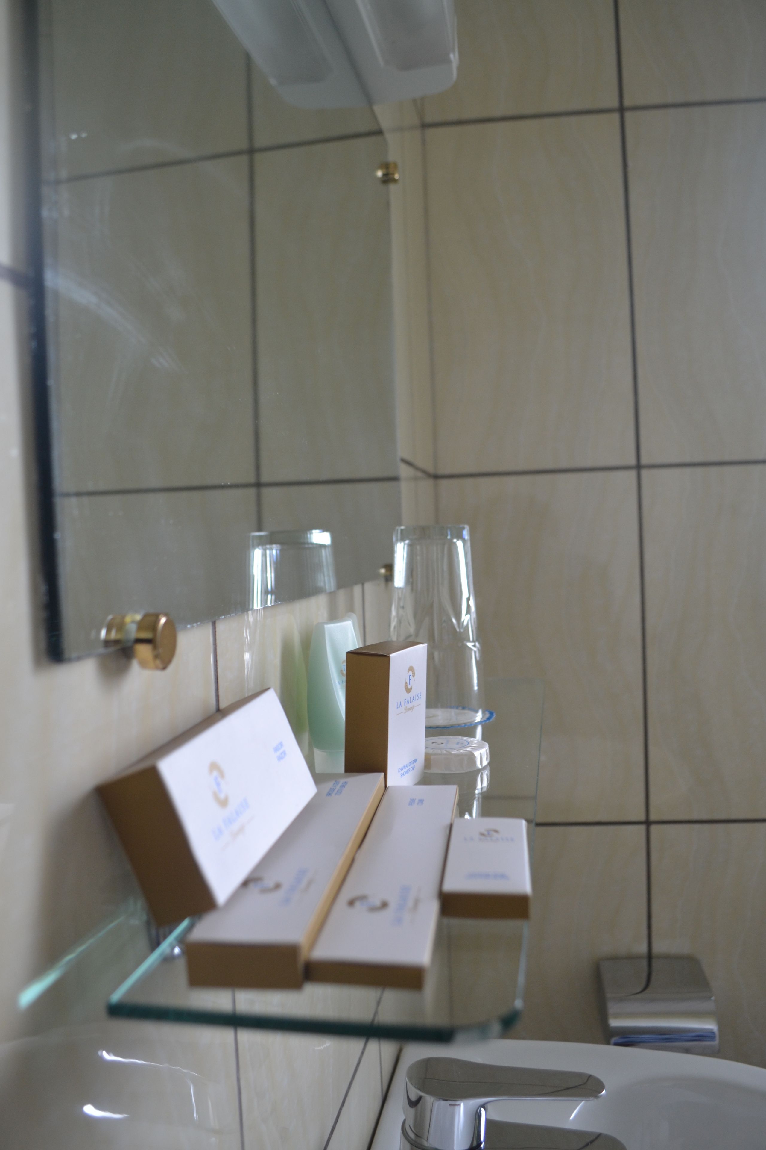 Casa de banho com prateleira de vidro com produtos de higiene e um espelho em cima.