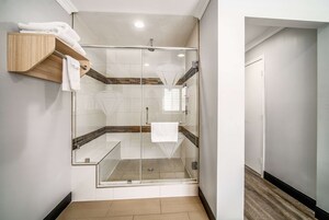 Um banheiro moderno com chuveiro em gabinete de vidro, um porta-toalhas de madeira e piso revestido com azulejos.