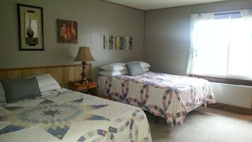Quarto com duas camas, uma mesa de cabeceira com abajur e janela com cortinas.