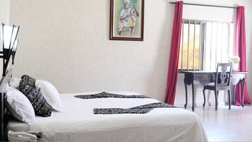 Quarto de hotel com cama, escrivaninha, cadeira, um quadro e janela com cortinas.
