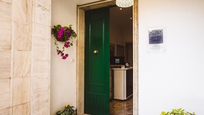 Uma porta verde com uma placa, um vaso de flores pendurado, uma pequena planta e uma luminária.