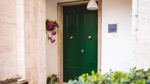 Uma porta verde com puxador de latão, um cesto de flores pendurado e uma placa na parede.