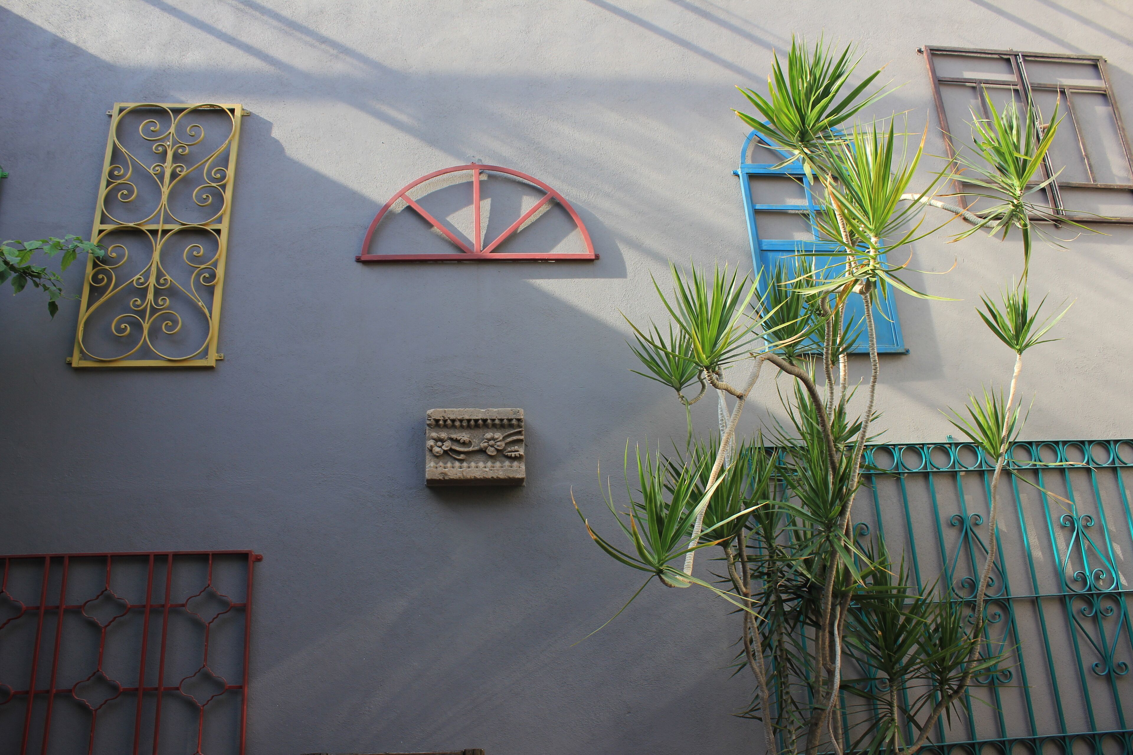 Fachada de edifício com grades de metal decorativas, uma placa de pedra e plantas em vasos.