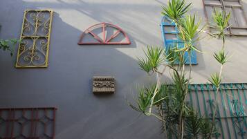 Fachada de edifício com grades de metal decorativas, uma placa de pedra e plantas em vasos.