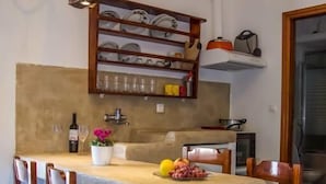 Uma cozinha com ilha central, cadeiras de madeira, luminária pendente e uma garrafa de vinho sobre o balcão.