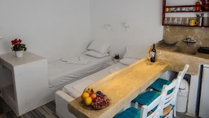 Espaço compacto com cozinha compacta, área de refeições com mesa comprida e cama com roupa de cama branca.