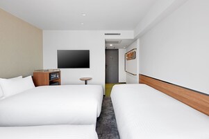 Quarto de hotel com duas camas, televisão, uma mesinha e um cabideiro.