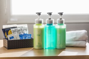 Um banheiro com toucador de madeira, uma toalha e três frascos de CUE hidratante corporal, shampoo e condicionador.
