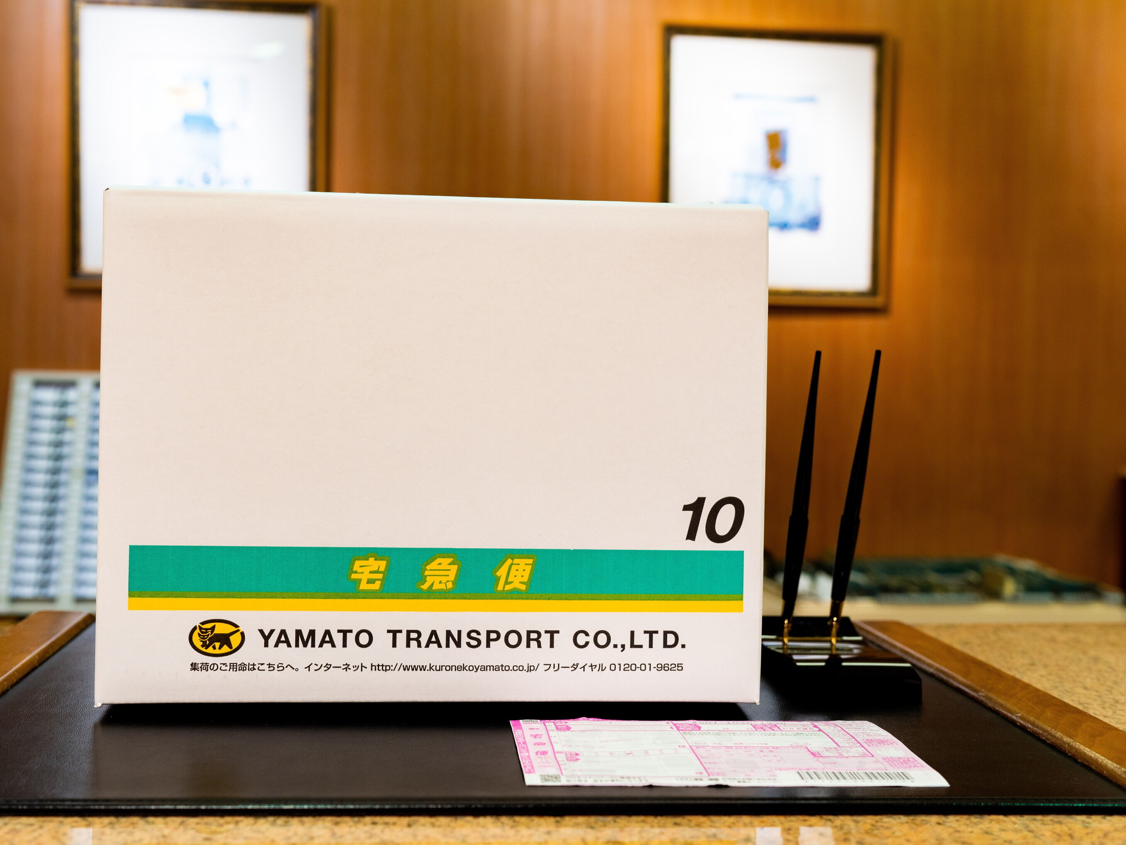 Placa da Yamato Transport Co., Ltd. com o número 10, colocada sobre um balcão com um recibo e um objeto preto ao lado.